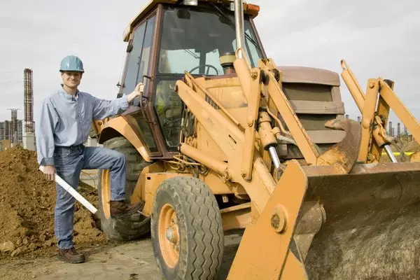 Portrait vun engem Bauaarbechter deen nieft engem Bulldozer steet